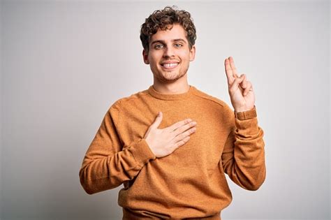 젊은 금발 잘생긴 남자 와 곱슬 머리 캐주얼 스웨터 위에 흰색 배경 미소 맹세 와 가슴과 손가락 충성 약속 선서 만들기 겨울에 대한 스톡 사진 및 기타 이미지 Istock