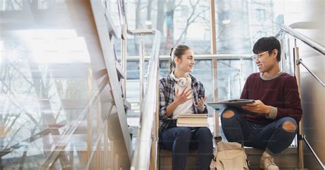 두 학생이 노트북과 책을 들고 계단에 앉아 대학 수업이 끝난 후 팀으로 프로젝트에 대해 논의하고 있습니다 사진