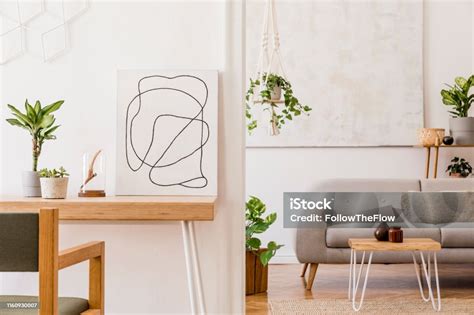 디자인 회색 소파 나무 책상과 커피 테이블 식물과 우아한 개인 액세서리와 아늑한 아파트에서 보헤미안 오픈 스페이스 인테리어 흰색 벽에 포스터 프레임을 조롱합니다 세련된 홈