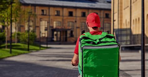 아름다운 햇볕이 잘 드는 거리를 따라 자전거를 타는 열 가방을 가진 남성 택배의 뒷모습 음식 배달 개념 사진 Unsplash의 산업 이미지