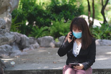 스마트 폰 태블릿을 사용하여 얼굴 마스크를 착용한 비즈니스 우먼은 일출과 자연 배경을 흐리게하는 공원에서 고객과 함께 일하십시오