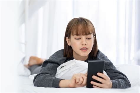 라이프 스타일 휴일 개념에서 소셜 미디어와 온라인 쇼핑 침실 미소와 행복에 소셜 미디어를 사용 하 여 Smartphone을 사용 하 여 흰색 침대에 누워 아름 다운 매력적인