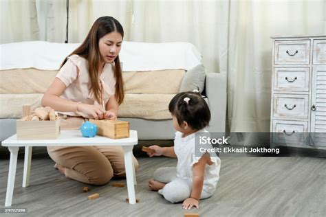 아시아 교사는 유치원에 들어가기 전에 아이들을 가르칩니다 유아가 바닥에 앉아서 나무 블록을 가지고 노는 동안 교사는 참여를 장려합니다 실습 학습은 인지 능력을 향상시킵니다