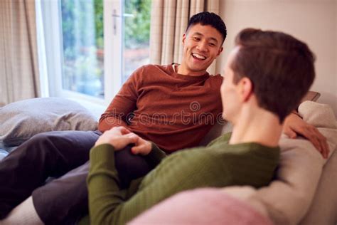 Loving Same Sex Male Couple Sitting On Sofa At Home Talking Together