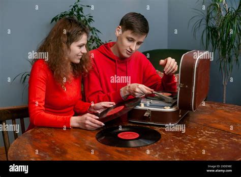 A Man And A Woman Are Seated At A Wooden Table With A Vintage Record Player Placed In Front Of