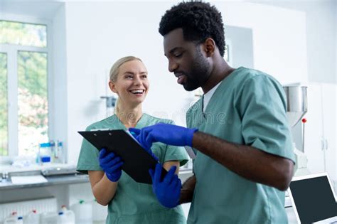 Woman Assistant Standing In Lab Discussing Papers With Multiethnic Man
