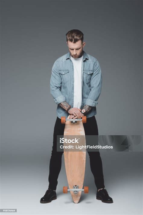 회색에 스케이트 보드와 함께 서 있는 잘생긴 젊은 문신된 남자의 전체 보기 남자에 대한 스톡 사진 및 기타 이미지 남자
