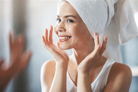 Pretty Lady Applying Cream Under Her Eyes After Shower Near Mirror At Home Stock Image Image