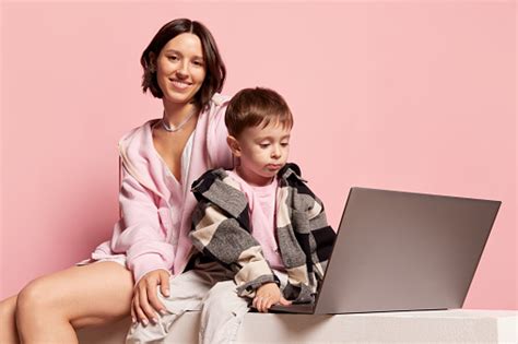 교육용 게임 젊은 여자와 어린 소년 엄마와 아들은 분홍색 스튜디오 배경에 고립된 노트북을 사용하고 있다 어머니의 날 축하 가족 어린 시절 모성의 개념 어머니에 대한 스톡