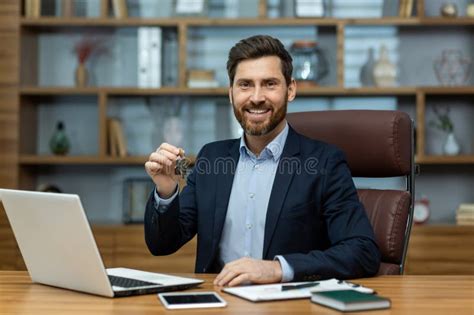 Happy Attractive Man In Shirt And Jacket Sitting By Desktop With Laptop And Holding Keys In Hand