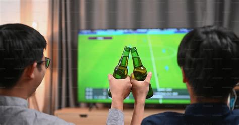 두 남자가 맥주 잔을 부딪치며 소파에서 축구를 응원하는 뒷모습 사진 Unsplash의 축구 팬 이미지