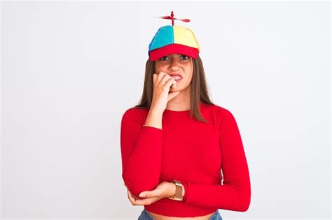 고립 된 흰색 배경 위에 서있는 프로펠러와 패니 캡을 입고 젊은 아름다운 소녀는 입물고 손톱에 손을 긴장 찾고 스트레스와 긴장