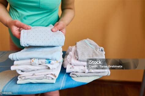 임산부 다리미판 옆에 서 있는 임산부 신생아를 위해 깨끗한 다림질 옷을 정리하는 모습 아기 의류에 대한 스톡 사진 및 기타 이미지 아기 의류 빨래 가사 집안일