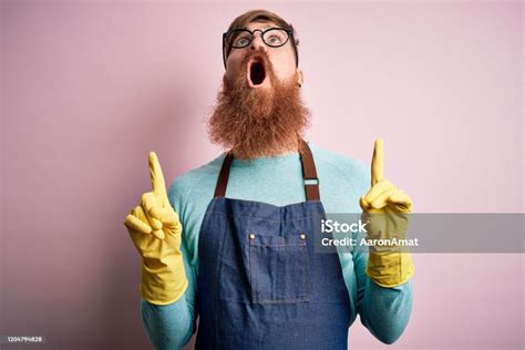 앞치마를 입고 장갑을 낀 수염을 가진 아이리쉬 레드헤드 하우스키핑 맨은 손가락과 팔을 들고 위를 올려다보고 놀랐습니다 가리키기에 대한 스톡 사진 및 기타 이미지 Istock