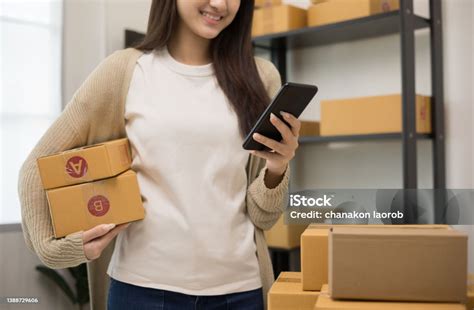 스마트 폰과 소포 종이 골판지를 들고 포즈를 취하는 기업가 서 있는 자세 집에서 일하는 상자가있는 여성 중소기업 소유자 배경에