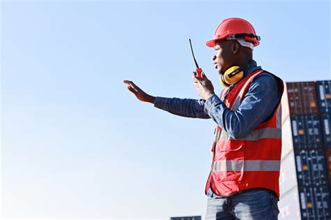 워키토키 무선 제어 적재 컨테이너 상자를 사용하는 감독 엔지니어 컨테이너 화물 현장에서 헬멧 작업을 통한 자신감 있는 엔지니어링 및 산업용 컨테이너 화물 운송 선박 점검