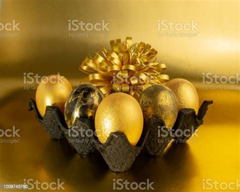 금색과 검은색으로 칠해진 다섯 개의 달걀은 반짝이는 배경에 어두운 질감의 스탠드에 놓여 있습니다 빛 부활절의 휴일 0명에 대한