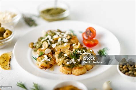 채식 음식 개념 향신료 치미추리 소스 아몬드 플레이크 올리브 튀긴 체리 토마토 케이퍼가 있는 콜리플라워 스테이크를 화이트 플레이트에 얹습니다 흰색 배경입니다 0명에 대한