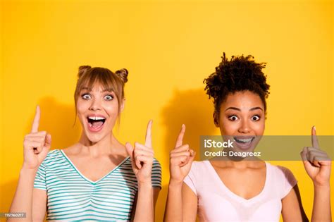 클로즈업 사진 아름 다운 두 사람 그녀의 모델 여자 긍정적 인 흥분 한 친구 펠로 우 다양성 인상 인덱스 손가락 착용 캐주얼 화이트 스트라이프 티셔츠 옷 고립 된 노란색
