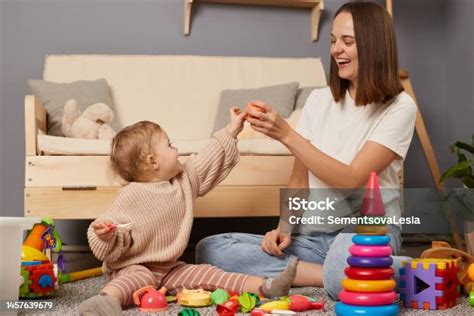 엄마와 딸이 기침 근처 바닥에 함께 앉아 장난감을 가지고 노는 실내 사진 엄마가 어린 아이와 즐거운 시간을 보내며 긍정적인 감정을 표현하는 장면 18 23 개월에 대한 스톡