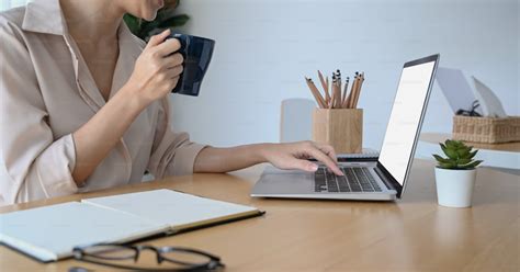 뜨거운 커피를 마시고 노트북 컴퓨터에서 일하는 웃는 사업가의 자른 가슴 사진 Unsplash의 테이블 이미지