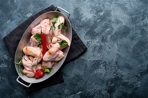 금속 팬 또는 어두운 회색 슬레이트 돌 또는 콘크리트 배경에서 요리하기위한 향신료와 재료와 그릇원시 닭 날개 검은 테이블에 향신료와 원시 고기 맨 위 보기입니다 모의