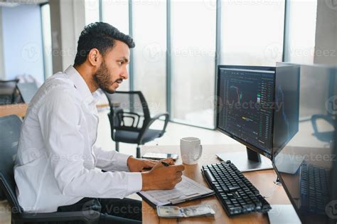 Side View Of Smart Indian Crypto Trader Investor Analyst Broker Using Laptop And Smartphone
