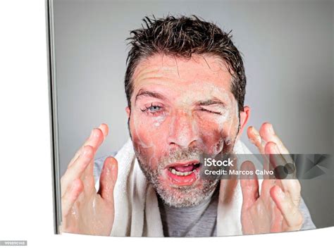 가려운 눈과 지저분한 얼굴 식 라이프 스타일 개념에 얼굴 피부 관리 치료를 적용 한 비누로 얼굴을 세척 하는 젊은 매력적이 고 재미 있는 남자의 거울 반사 초상화 30 39