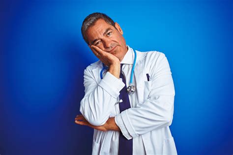잘 생긴 중년 의사 남자 고립 된 푸른 배경 에 청진기를 입고 피곤 하 고 교차 된 팔을 가진 우울증 문제로 지루 해 보이는 생각 건강관리와 의술에 대한 스톡 사진 및 기타