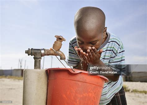 Young Boy Drinking Water From A Bucket At A Communal Township Tap