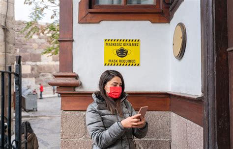 보호 얼굴 마스크를 가진 젊은 여성 관광객이 보호 면 마스크를 착용하고 스마트 폰을 확인하는 역사적인 레스토랑 입구로 계단을 오르고 있습니다 35 39세에 대한 스톡 사진