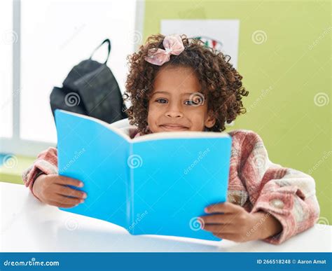 African American Girl Reading Book Sitting On Table At Classroom Stock