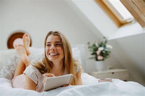 Premium Photo Young Happy Woman Making Notes In Note Pad While Sitting On Bed At Home