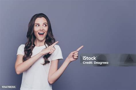 아름 다운 사랑 스러운 사랑 스러운 세련 된 명랑 기쁘게 곱슬 머리 여자 캐주얼 화이트에의 T셔츠 옆 두 손으로 가리키는 입을 복사공간 회색 배경 위에 절연 T 셔츠에 대한