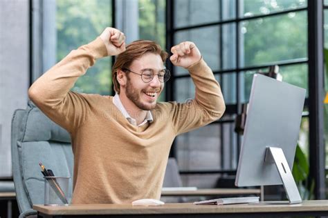Smiling Young Male Programmer Freelancer Sits At The Table Looks Happy At The Computer Monitor