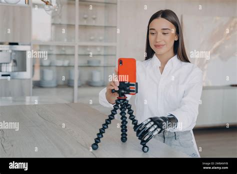Smiling Woman With A Prosthetic Arm Setting Up A Mobile Phone On A Tripod For A Video Call In A