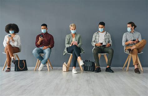 스튜디오에서 회색 배경에 대한 인터뷰를 위해 대기 줄에 앉아있는 동안 마스크 착용 비즈니스 사람들의 다양한 그룹의 전체 길이 샷 채용에 대한 스톡 사진 및 기타 이미지