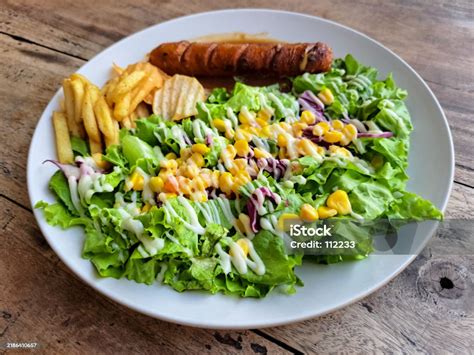 구운 소시지 알래스카 소시지 감자 튀김 양상추 얇게 썬 양파 양상추 삶은 옥수수 커널 씨앗 가지 당근 후추 소스 및 마요네즈 소스를 곁들인 접시 서양 음식 메뉴 0명에 대한