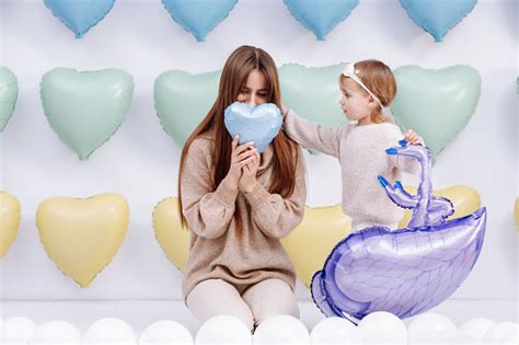 아름다운 젊은 어머니와 작은 귀여운 딸이 함께 재미를 가지고 화려한 심장 풍선 배경에 서서 포옹하고 키스합니다 생일 벨렌틴 어머니의 날 2 3 살에 대한 스톡 사진 및 기타