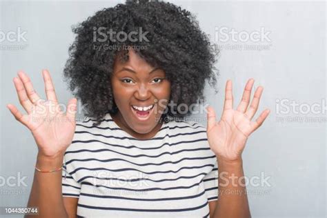 젊은 아프리카계 미국인 플러스 크기 여자에 회색 그런 지 벽 축 화 하 고 무기와 성공에 대 한 미친 제기 흥분 비명 눈을 폐쇄 우승자 개념 T 셔츠에 대한 스톡 사진 및