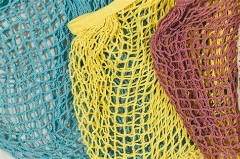 베이지 색 배경에 파란색 노란색 분홍색 베이지 색 재사용 가능한 면 메쉬 가방 친환경 쇼핑백 닫습니다 제로 폐기물 식료품 개념 플라스틱이 없는 지속 가능한 라이프스타일 0에