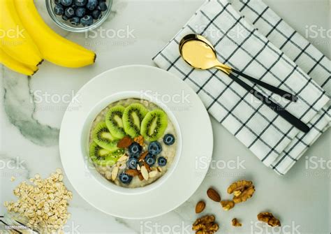 건강한 아침 식사 대리석 조리대에 흰색 그릇에 키위 블루베리 견과류가 있는 오트밀 죽 오트밀 플레이크 잘 익은 바나나 맨 위