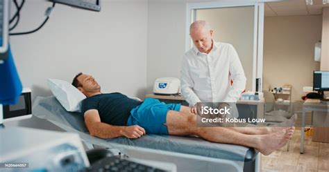 병원 시험 상담에서 다리 또는 근육통에 대한 물리 치료 환자가있는 물리 치료사 의사 정형 외과 테이블에서 스포츠 남자의 검사를하는 수석 건강 관리 전문가 무릎에 대한 스톡