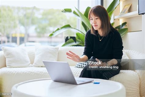 중국 사업가가 창가 소파에 앉아 노트북을 사용하여 화상 회의를 위해 온라인에 접속하고 있다 40 44세에 대한 스톡 사진 및