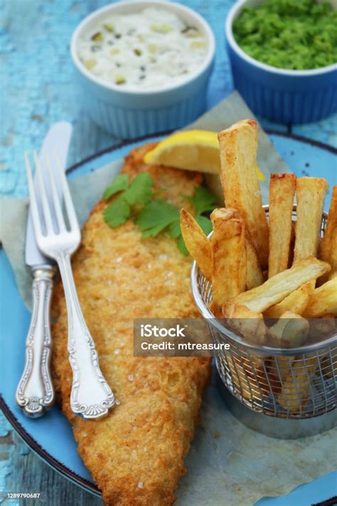 기름진 양피지 칼과 포크 레몬 슬라이스 타르타르 소스와 무시 완두콩을 함유 한 그릇 청록색 나무 곡물 배경 높은 전망과 청록색 접시에 파슬리로 장식 된 피시 앤 칩스 의