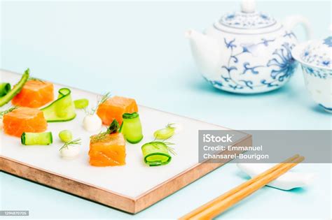 아스파라거스 에다마메 콩 크림 치즈 호박이 달린 생 연어의 주사위는 중국 주전자와 파란색 배경에 젓가락을 얹은 대리석 접시에 놓입니다 공간을 복사합니다 측면 상단 보기입니다