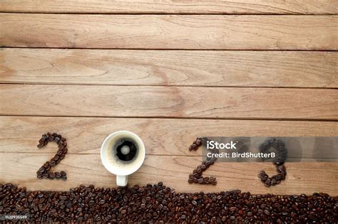 거품이있는 하얀 컵에 커피 원두와 뜨거운 신선한 커피의 톱 뷰와 새해 복 많이 받으세요 컨셉을위한 텍스트 2023 나무 테이블