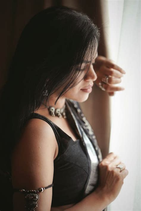 창문 옆의 전통 인도 의상을 입은 우아한 여성 · 무료 스톡 사진