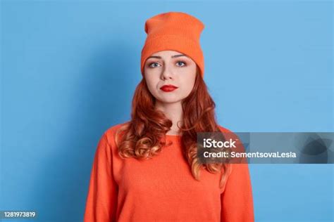 모자를 쓴 심술궂은 무디소녀의 초상화와 파란 배경위에 고립된 카메라를 바라보는 따뜻한 점퍼 곱슬머리와 빨간 입술을 가진 여성