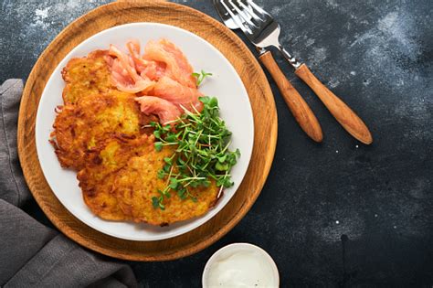 감자 팬케이크 오래된 검은 테이블 배경에 소박한 접시에 크림 파 마이크로 그린 붉은 연어와 소스와 함께 집에서 만든 감자 팬